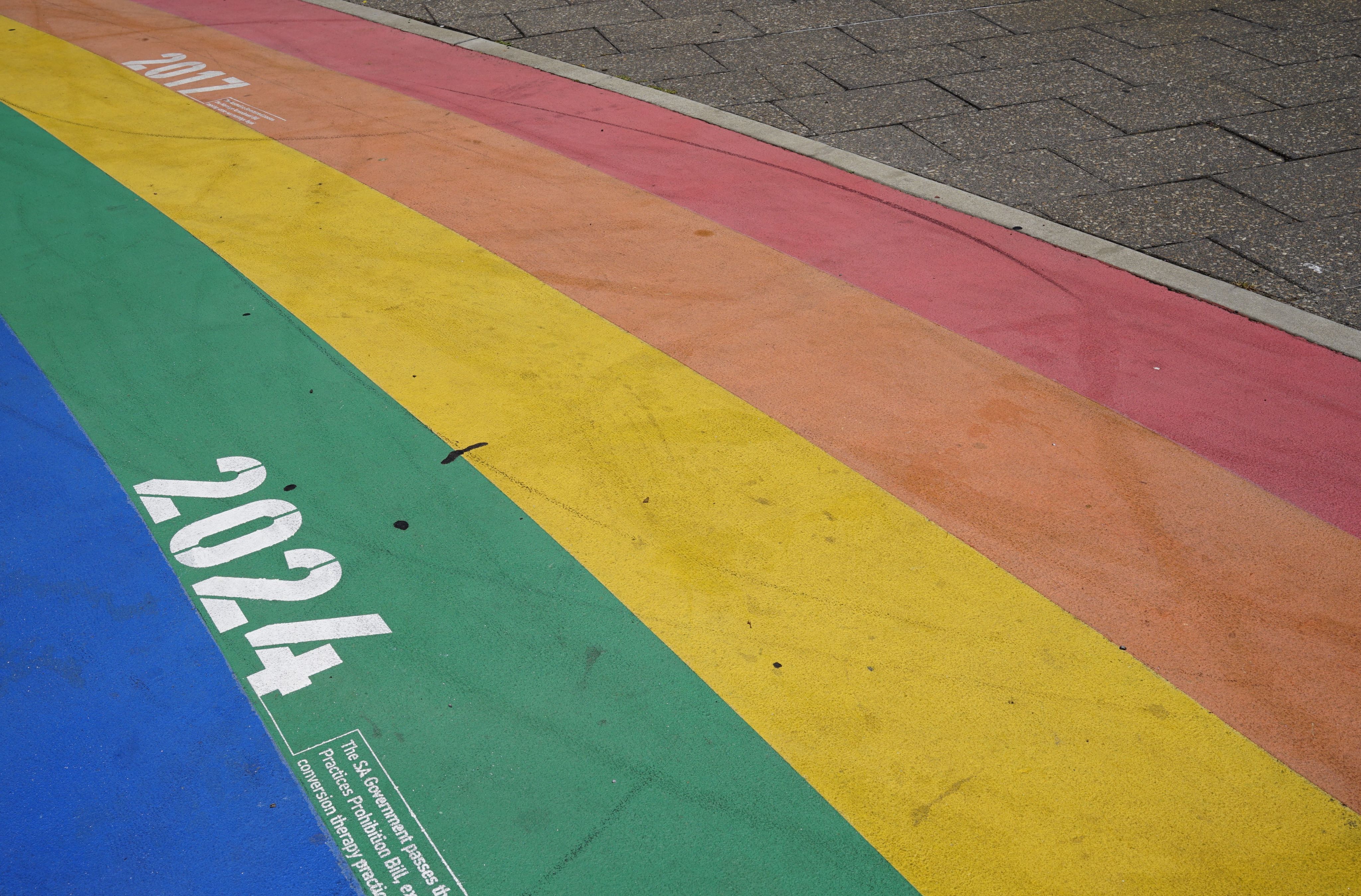 Part of a rainbow painted on the pavement. In the bottom left corner ...