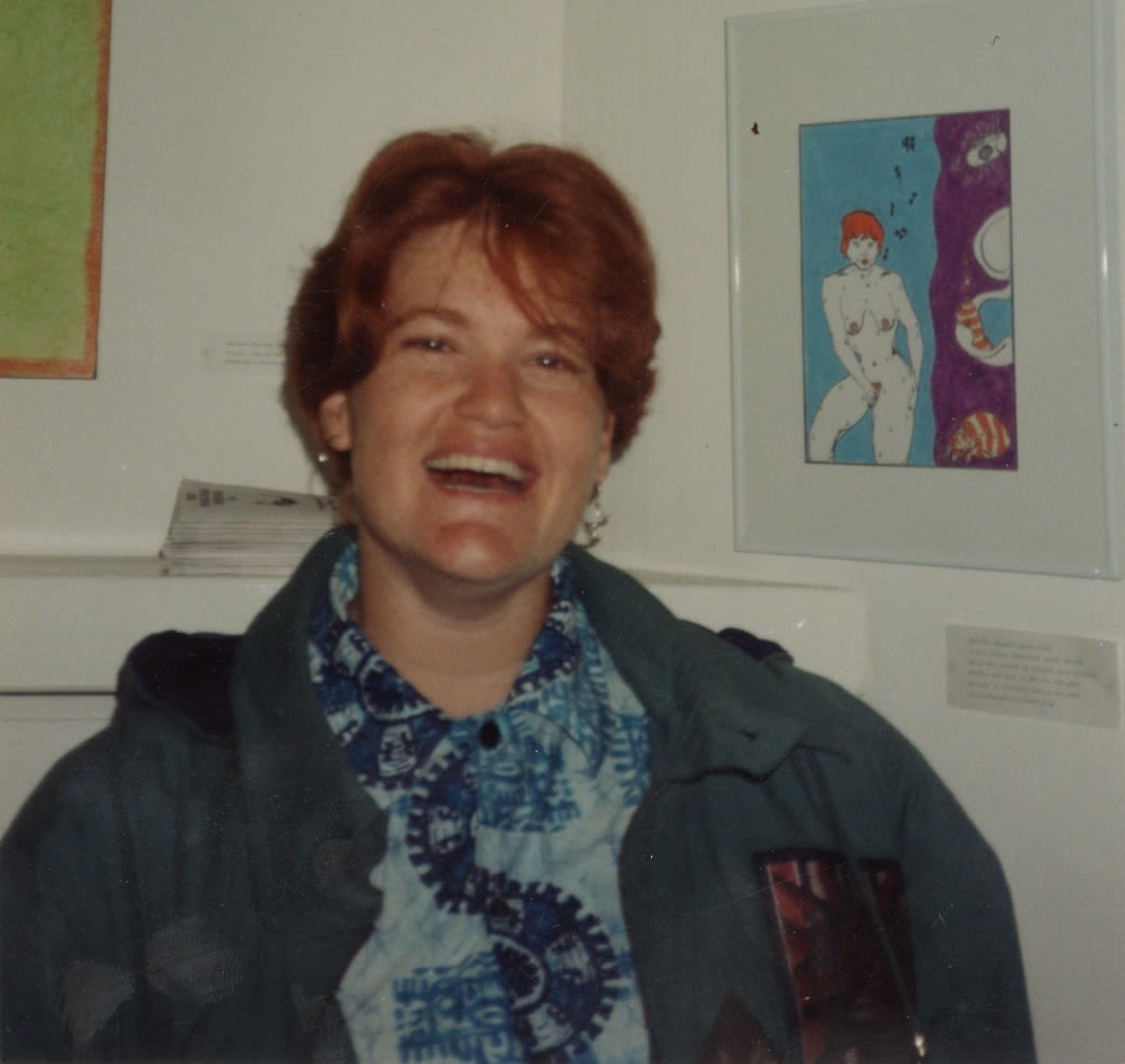 A woman with cropped red hair smiles at the camera. Behind her is an ...
